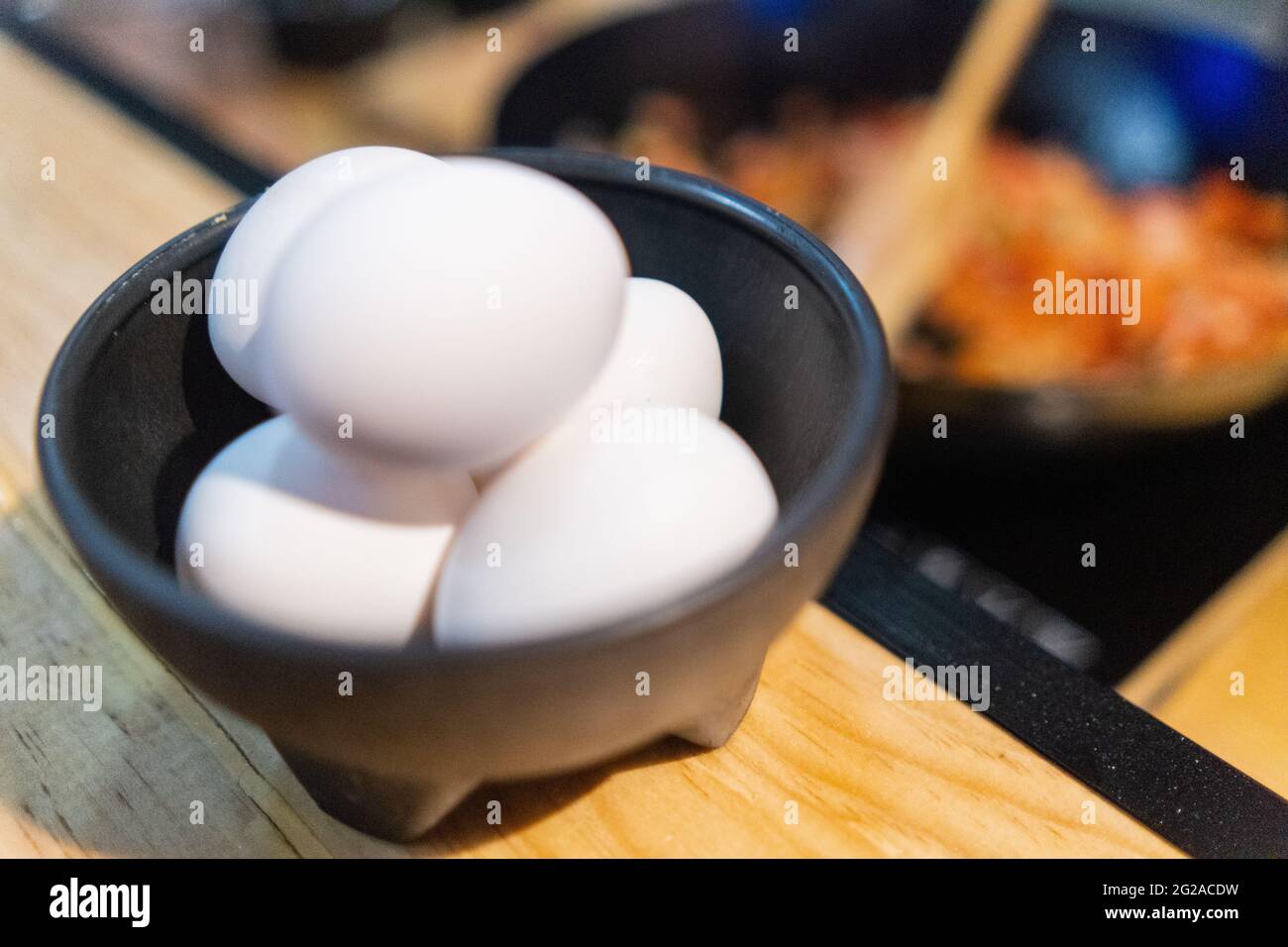 Eggs in small black bowl with blurry food in pan as background Stock ...