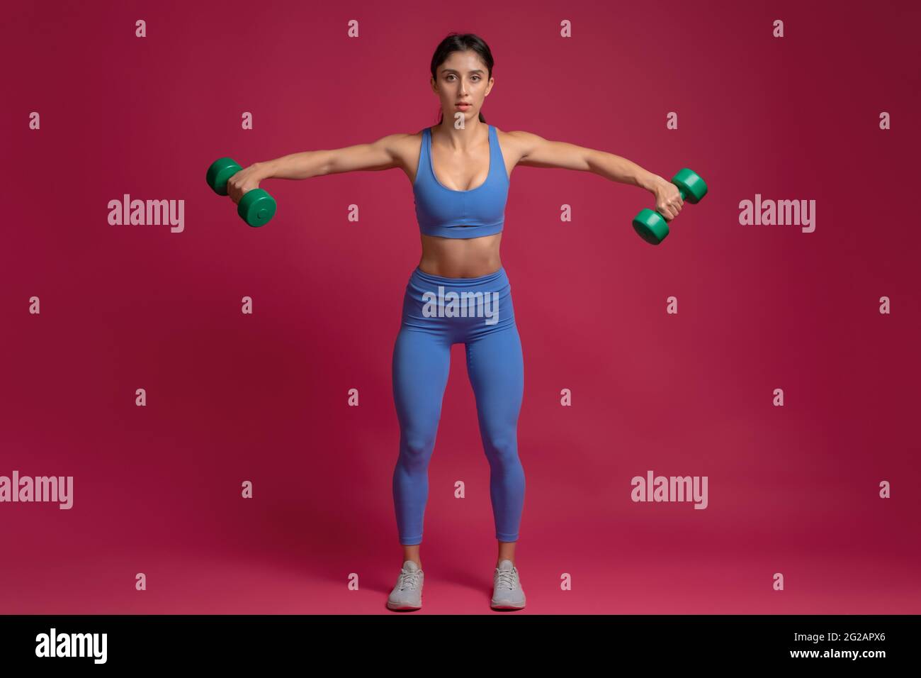 Girl performing dumbbell lateral raise on maroon background Stock Photo ...