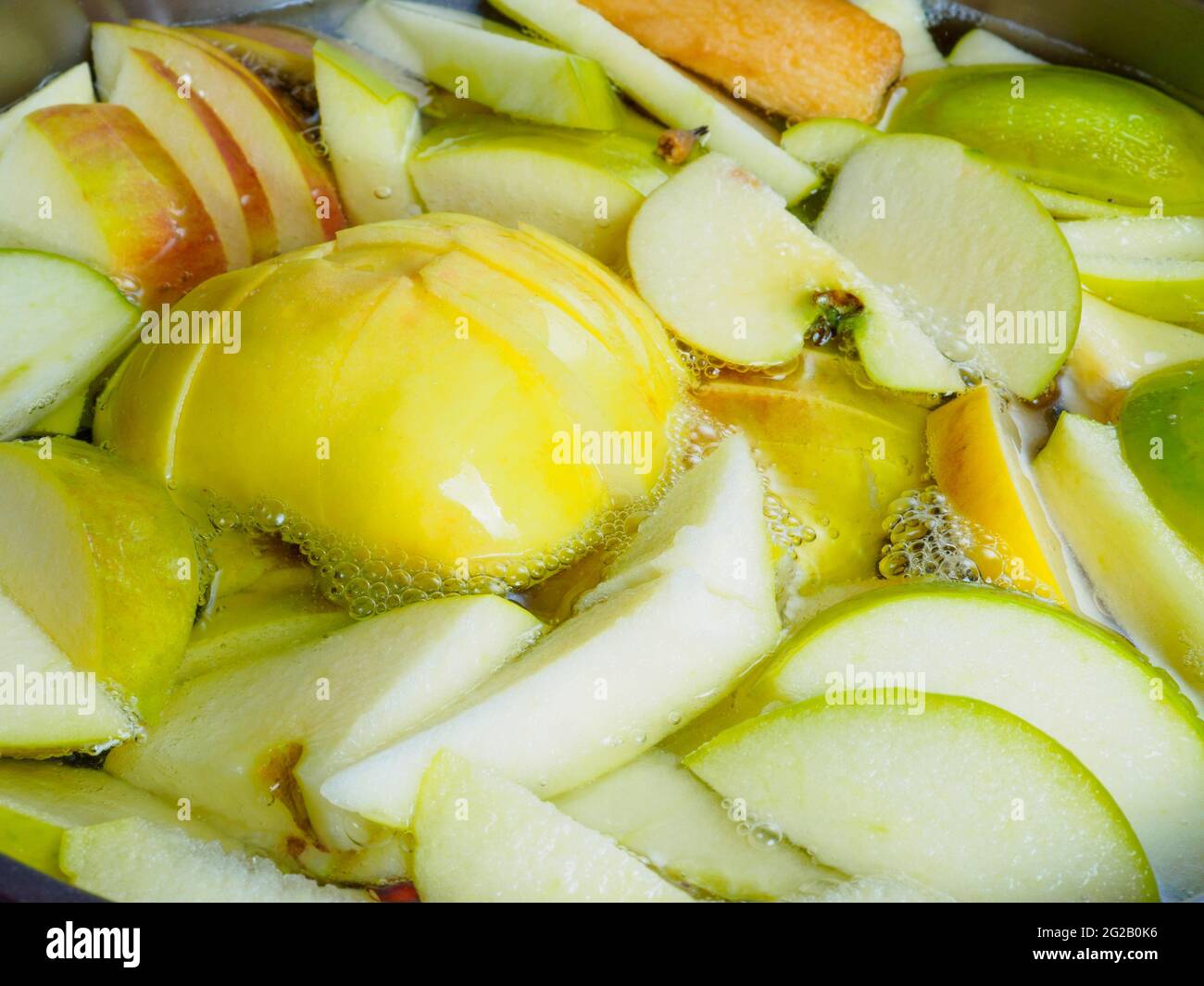 Close-up of the pieces of yellow and green apples in boiling water. The ...