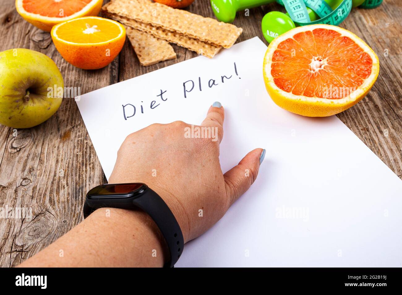 Female hand shows the diet plan. Healthy food, dumbbells and measuring ...
