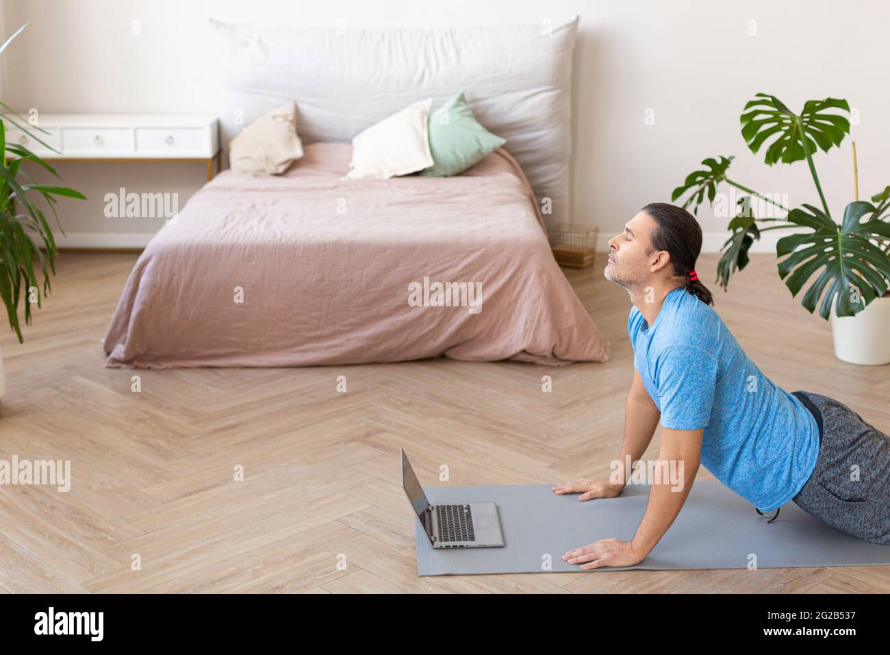 Health care concept - man practices yoga at home in front of a laptop ...