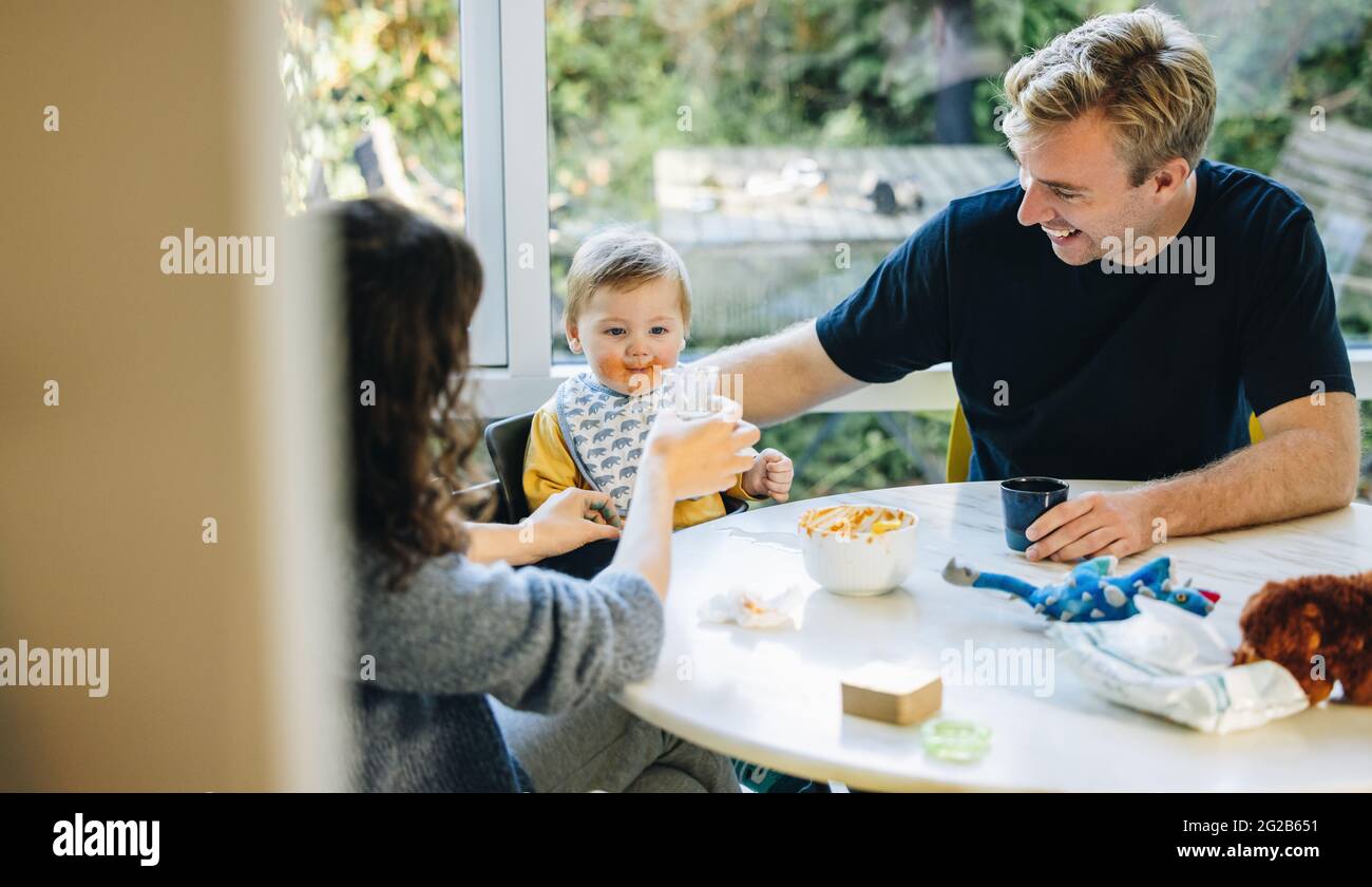 Parents feeding baby at home. Mother and father sitting at table and ...