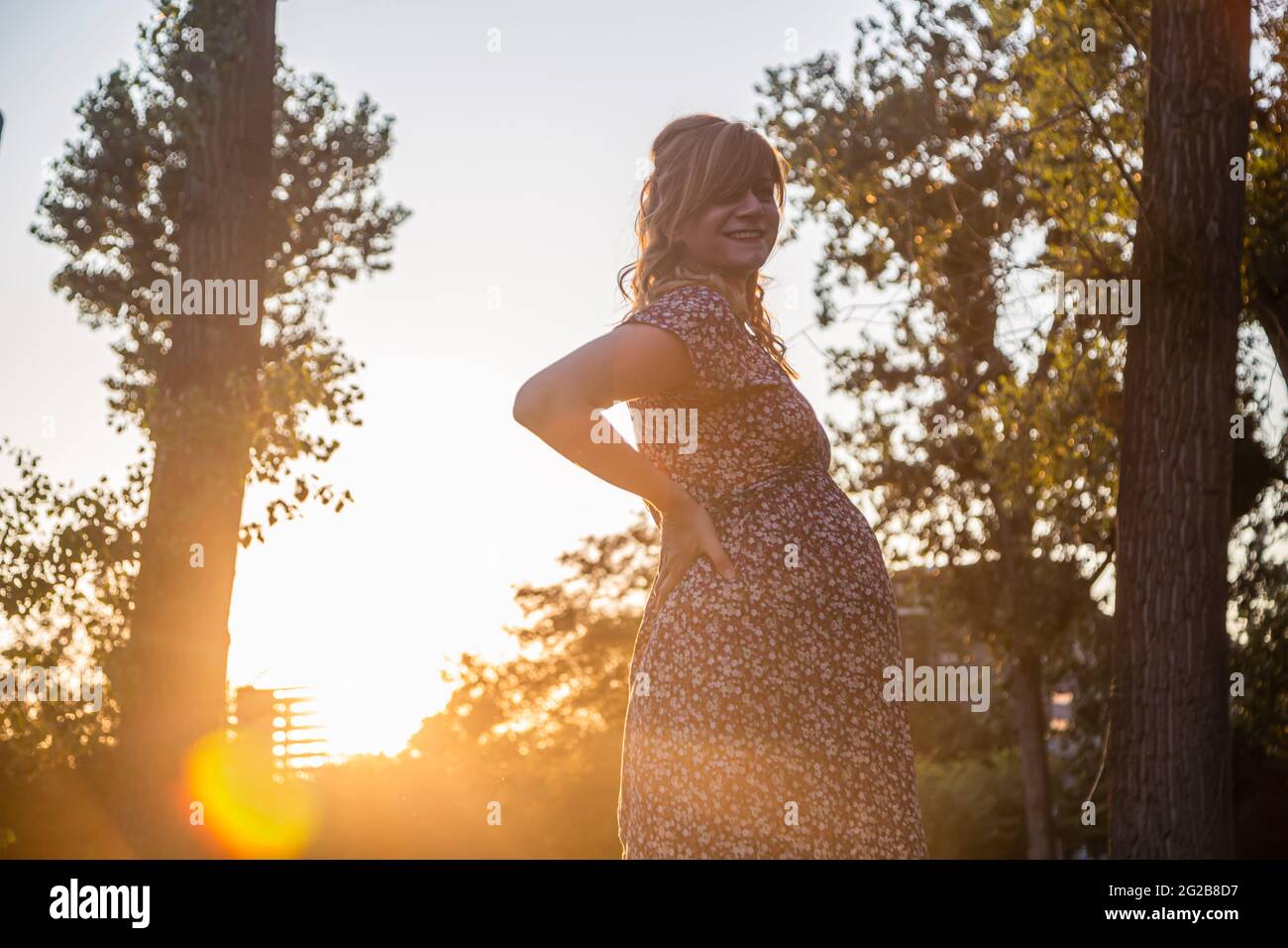 A happy caucasian pregnant woman in the city park during sunset with ...