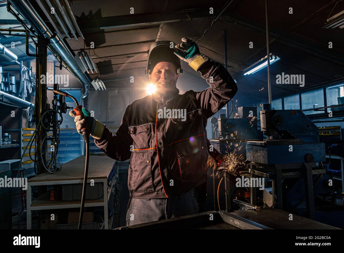 Portrait of a smiling welder posing in workshop while his colleague in ...