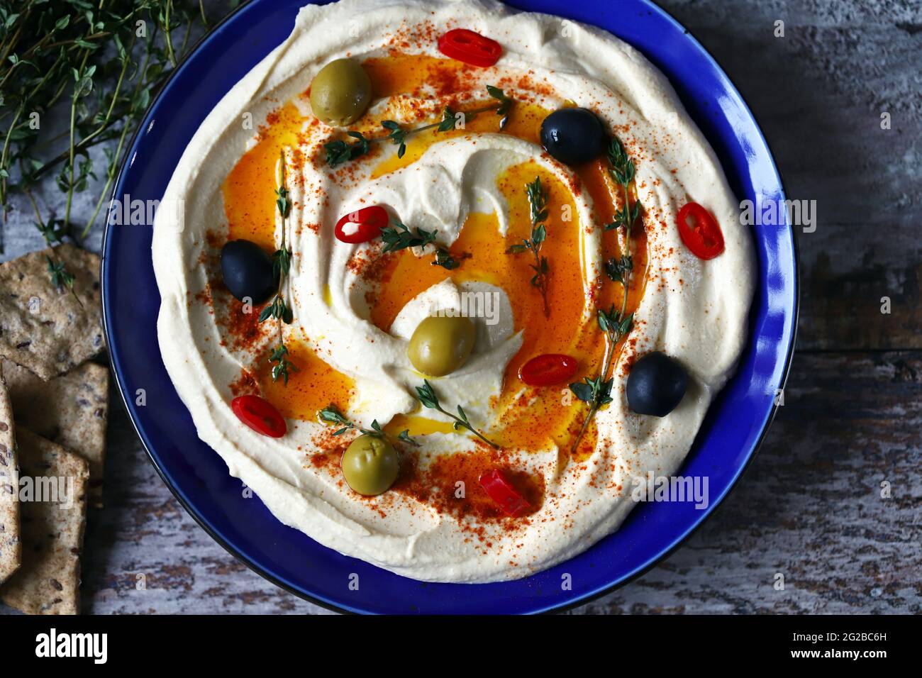 Hummus with olives, paprika and olive oil in a blue plate. A ...