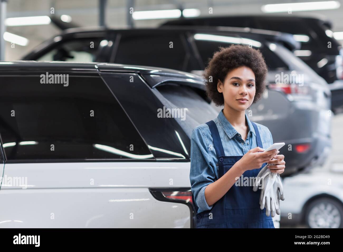 positive young african american mechanic in overalls standing with ...