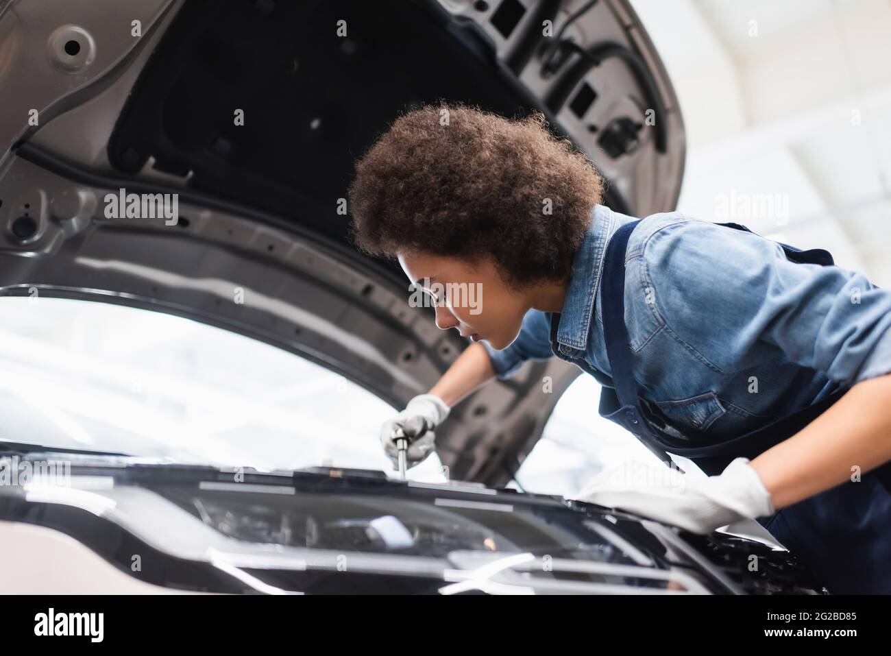 young african american mechanic fixing motor in car with open hood in ...