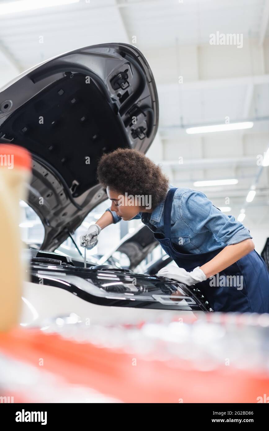 young african american mechanic fixing motor in car with open hood in ...