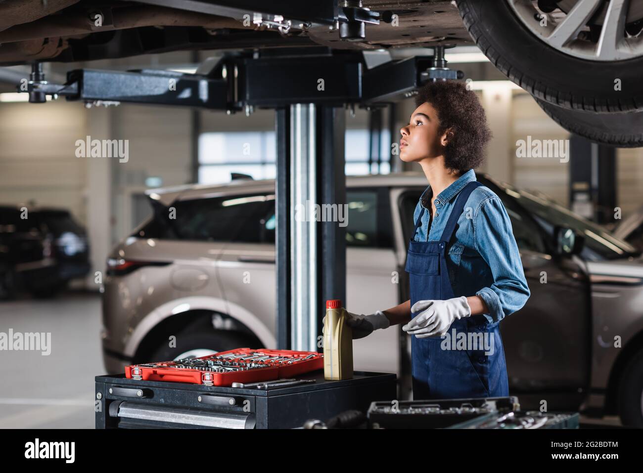 focused young african american mechanic standing underneath car and ...