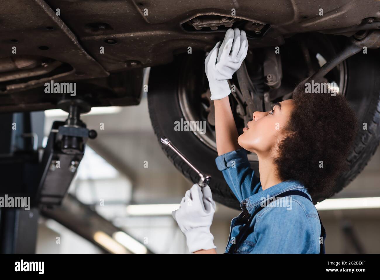 young african american mechanic with wrench repairing bottom of lifted ...