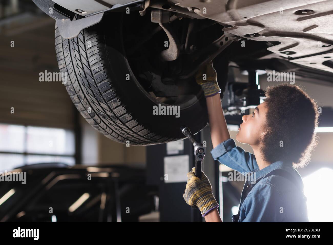 young african american mechanic with wrench repairing wheel of lifted ...