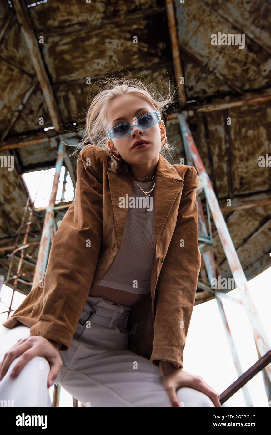 low angle view of pretty young model in blue sunglasses, white pants ...