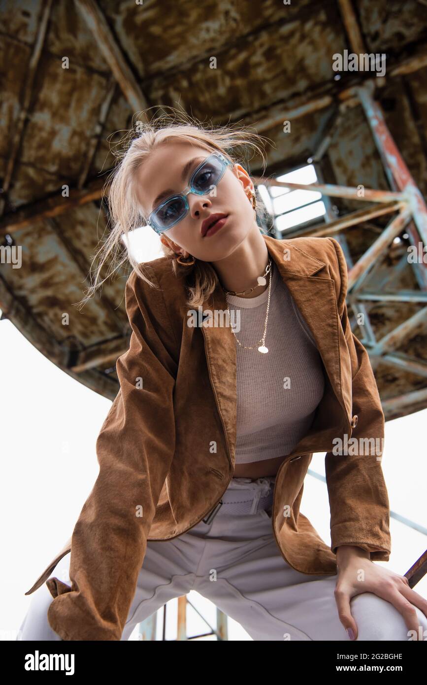 low angle view of pretty young model in blue sunglasses looking at ...