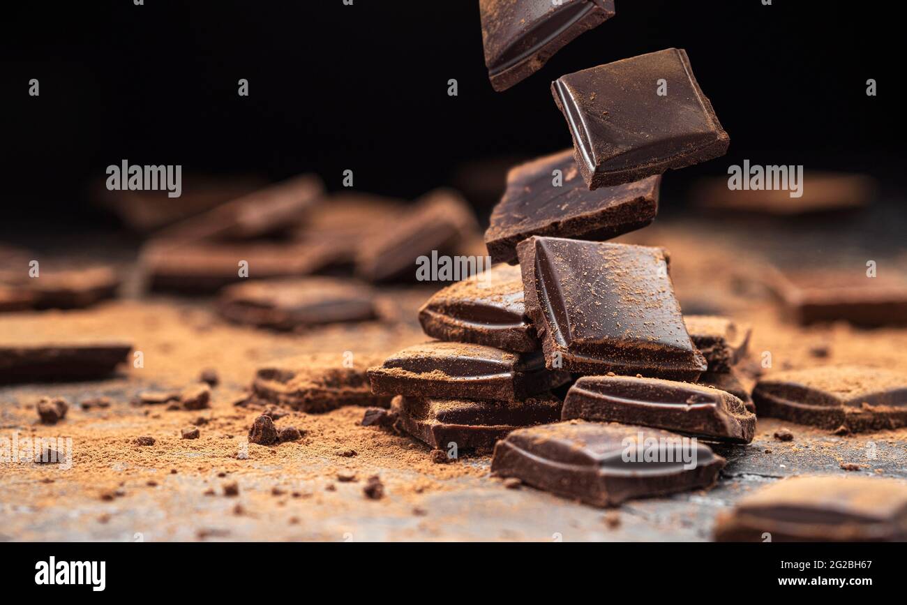 Falling broken chocolate bars on black slate background with cocoa ...