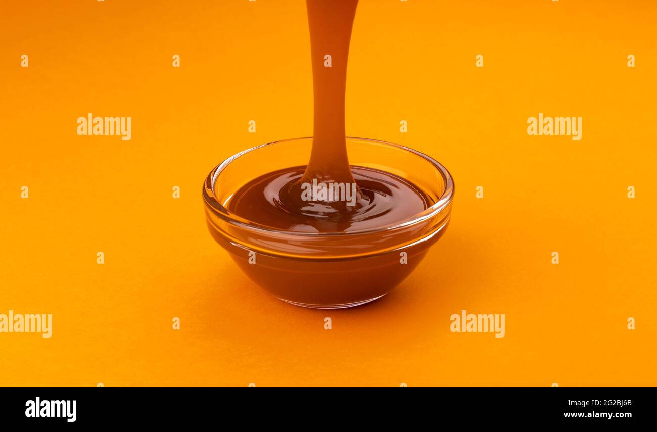 Pouring caramel sauce in glass bowl on color background Stock Photo - Alamy
