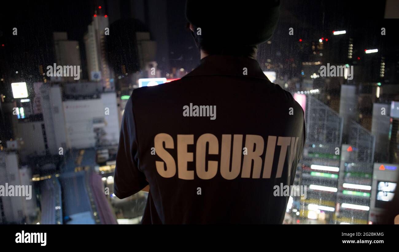 Closeup shot of a security guard looking down the city full of lights ...
