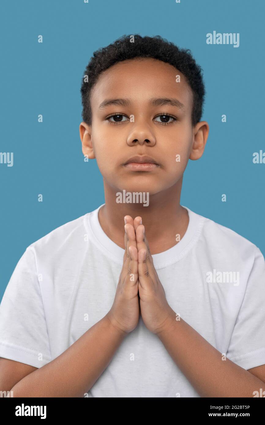 Serious bdark skinned boy standing in namaste Stock Photo - Alamy
