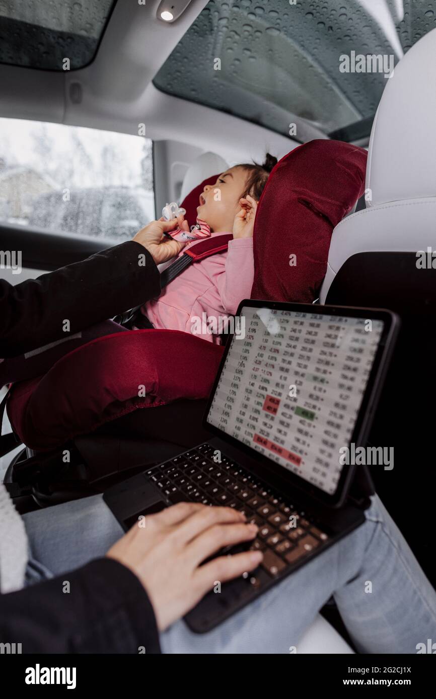 Baby girl sitting in car seat while mother using laptop Stock Photo - Alamy