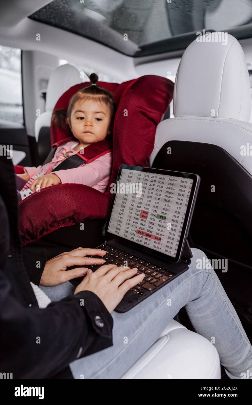 Baby girl sitting in car seat while mother using laptop Stock Photo - Alamy