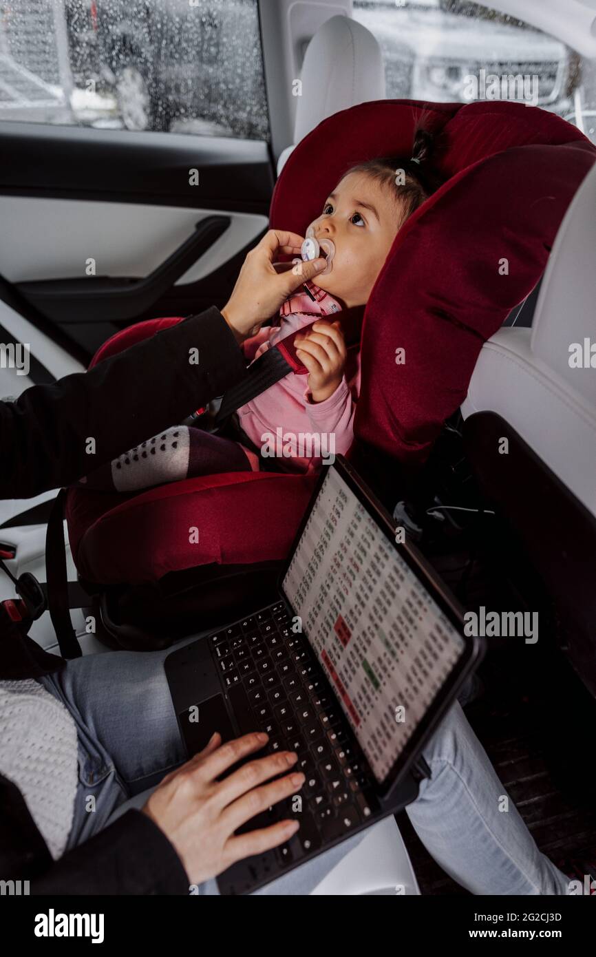 Baby girl sitting in car seat while mother using laptop Stock Photo - Alamy