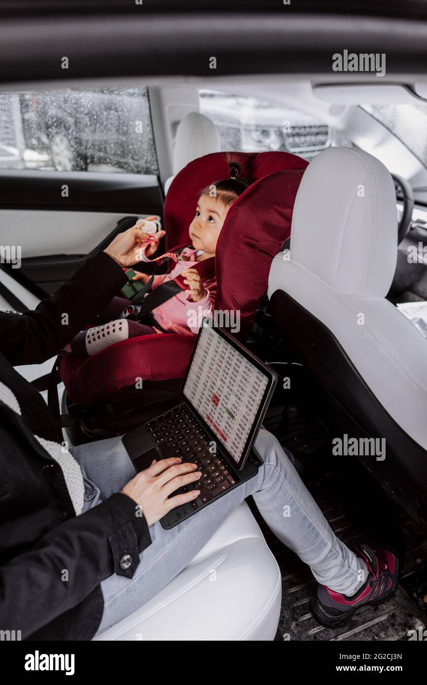Baby girl sitting in car seat while mother using laptop Stock Photo - Alamy
