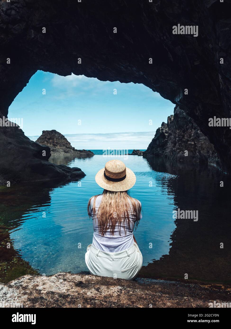 Vertical shot of a female from back sitting on the stone and looking at ...