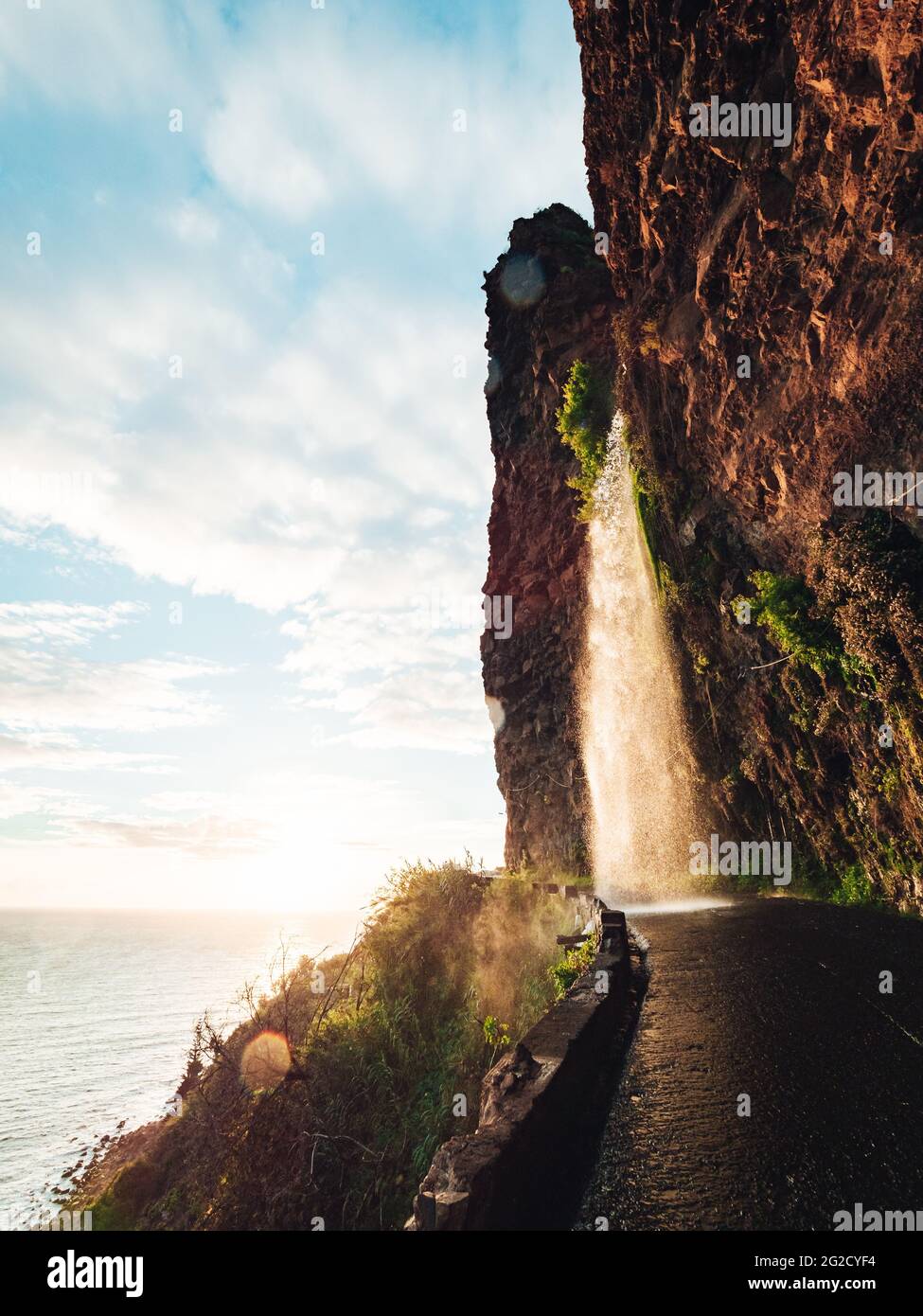 Vertical shot of a waterfall flowing out from the rocks near the sea under a cloudy sky Stock ...