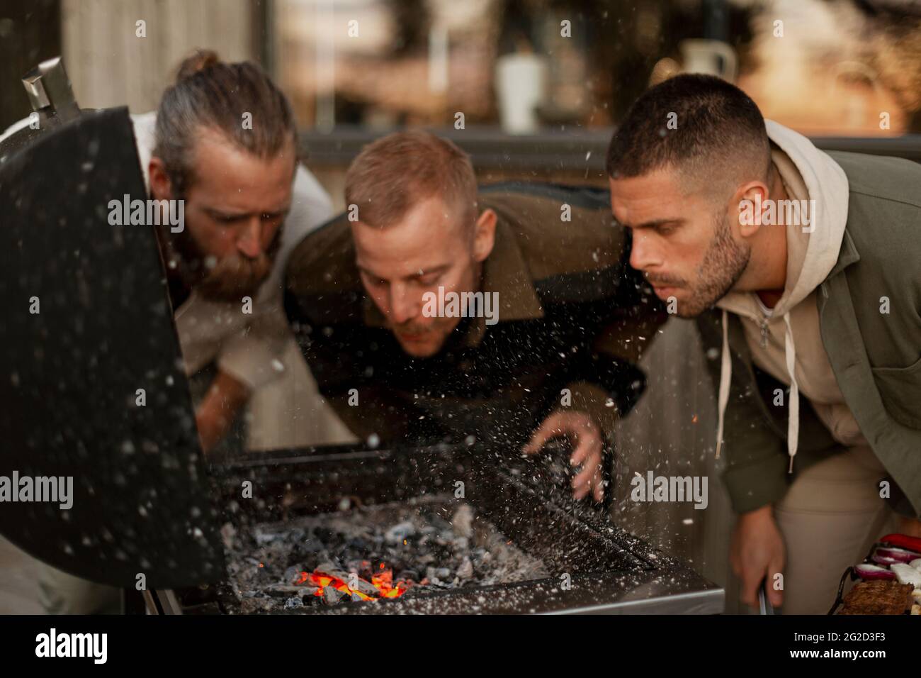 Male friends blowing on barbecue Stock Photo - Alamy