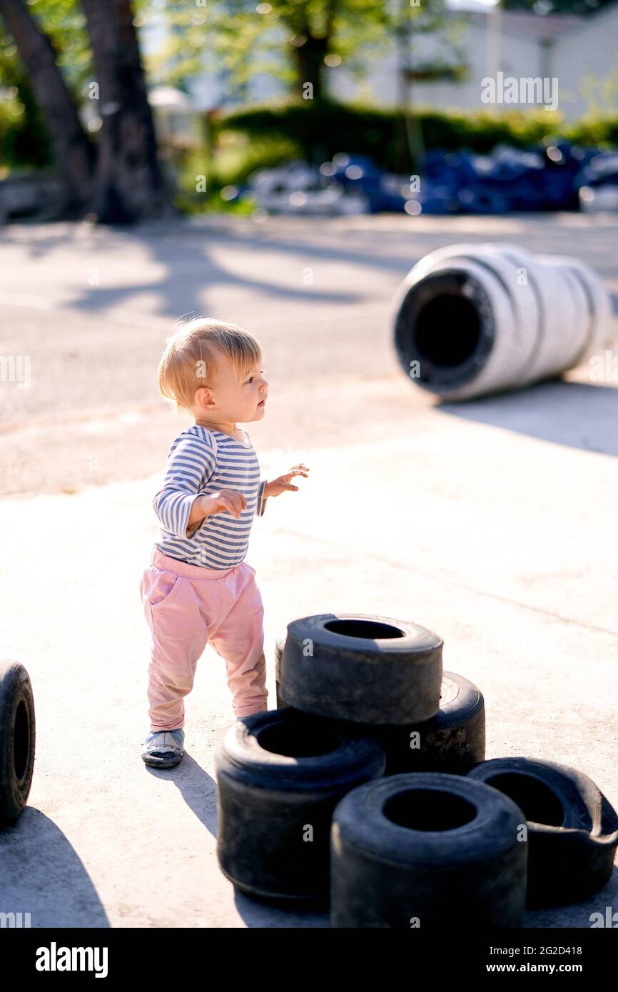 Kid stands sideways near the piled-up car tires in the parking lot ...