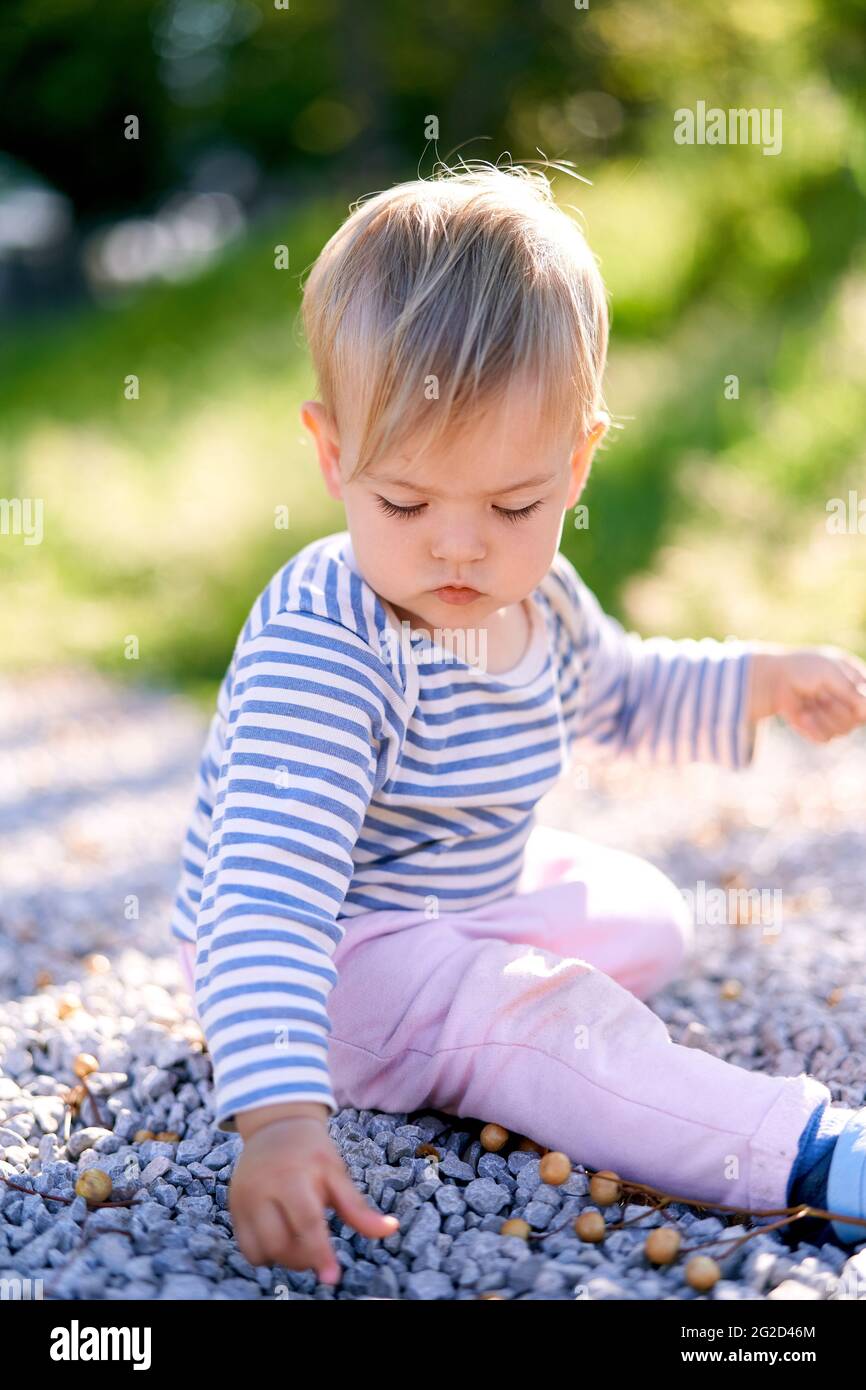 Kid sits on a gravel path and reaches for a pebble Stock Photo - Alamy