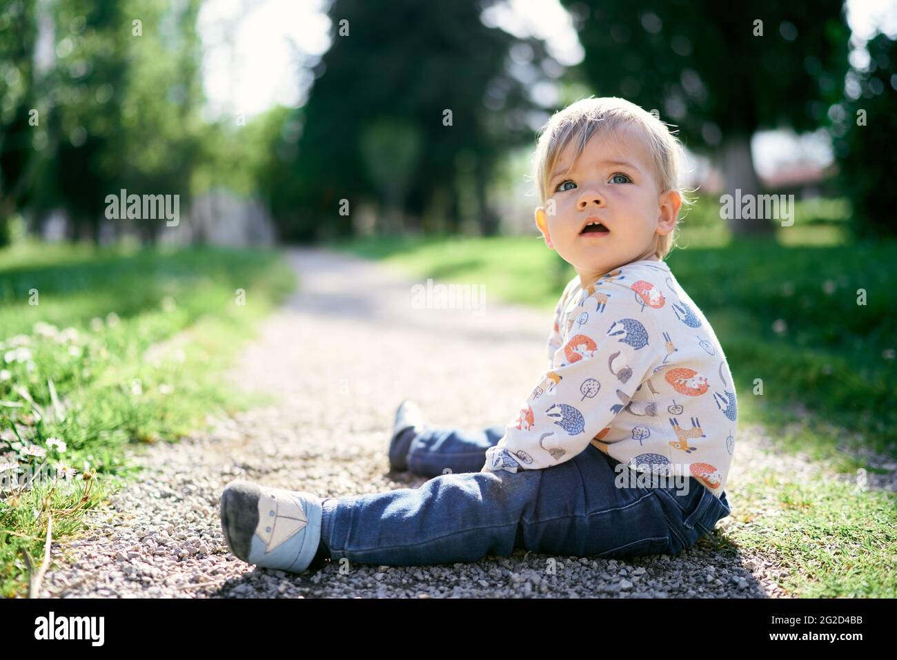 Kid sits on the path in the park, turning his head to the side Stock ...