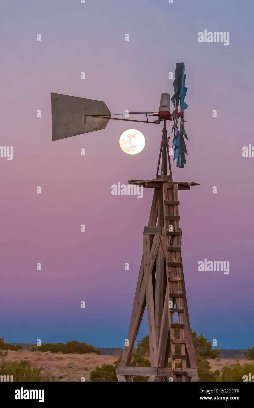 Vertical shot of an old windmill with the full moon in the colorful sky ...