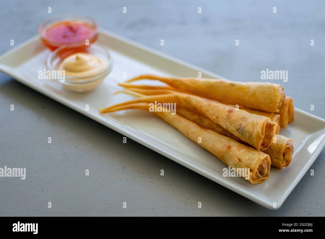 a plate of delicious prawn spring rolls served with dipping sauces on a ...