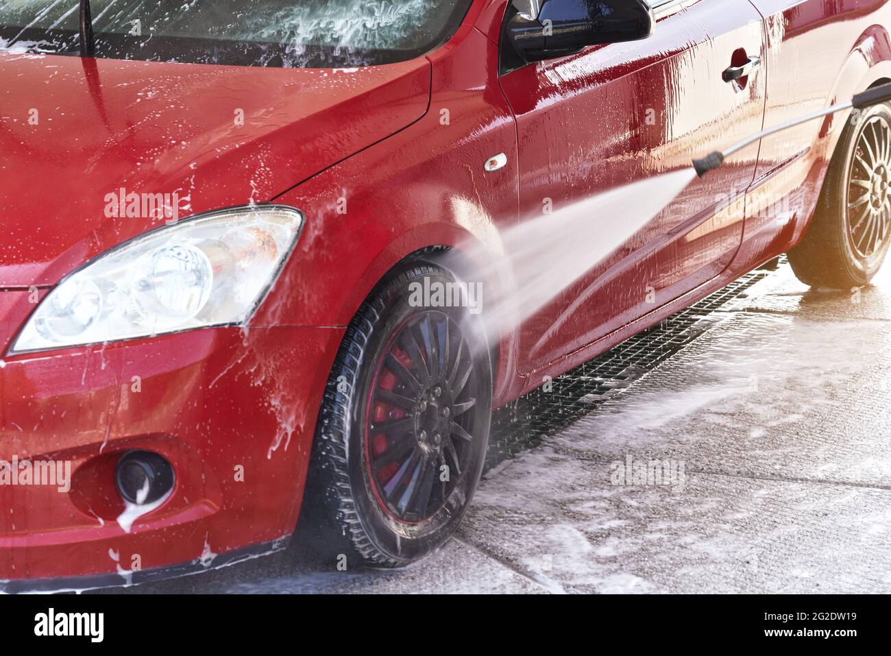 Front light of red car washed in self serve carwash, liquid reflected ...