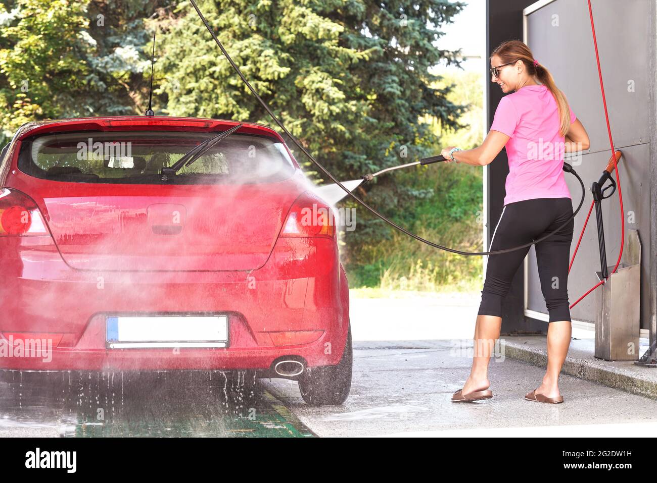 Young woman washing her red car in self serve carwash, view from back ...