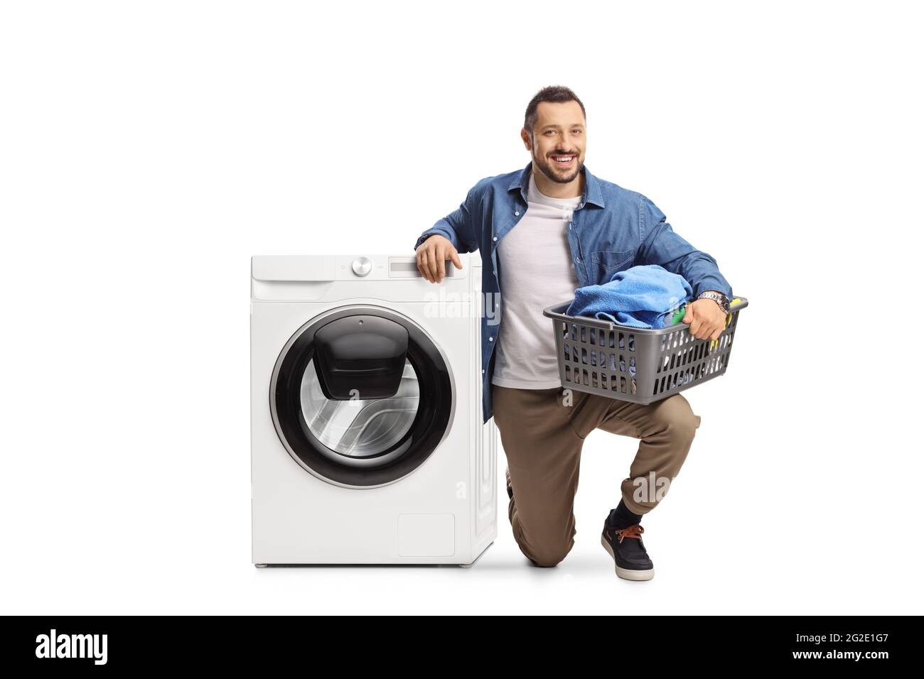 Smiling young man kneeling next to a washing machine and holding a ...