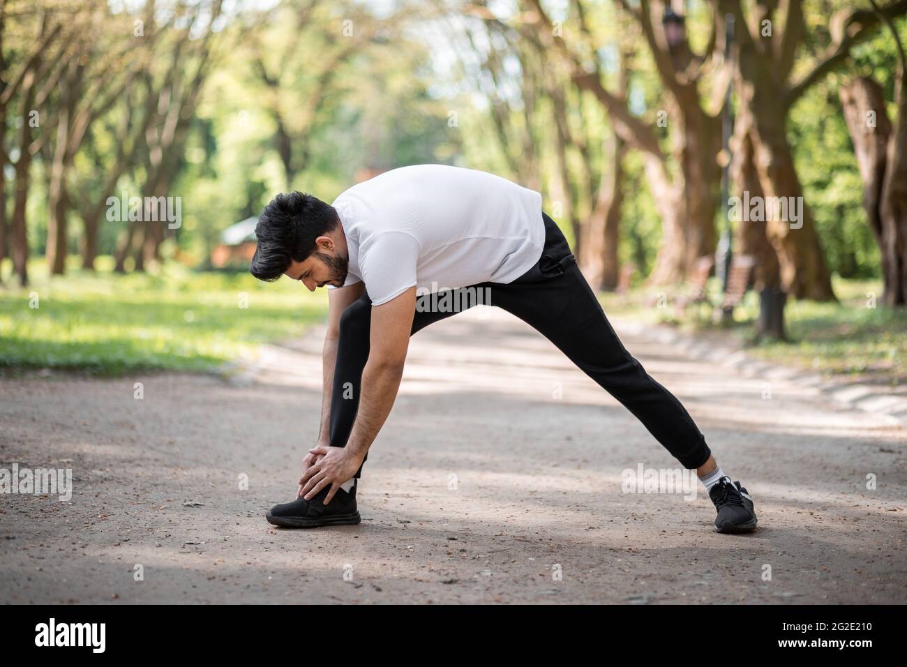 Healthy muslim guy in sport outfit doing flexible exercises outdoors ...