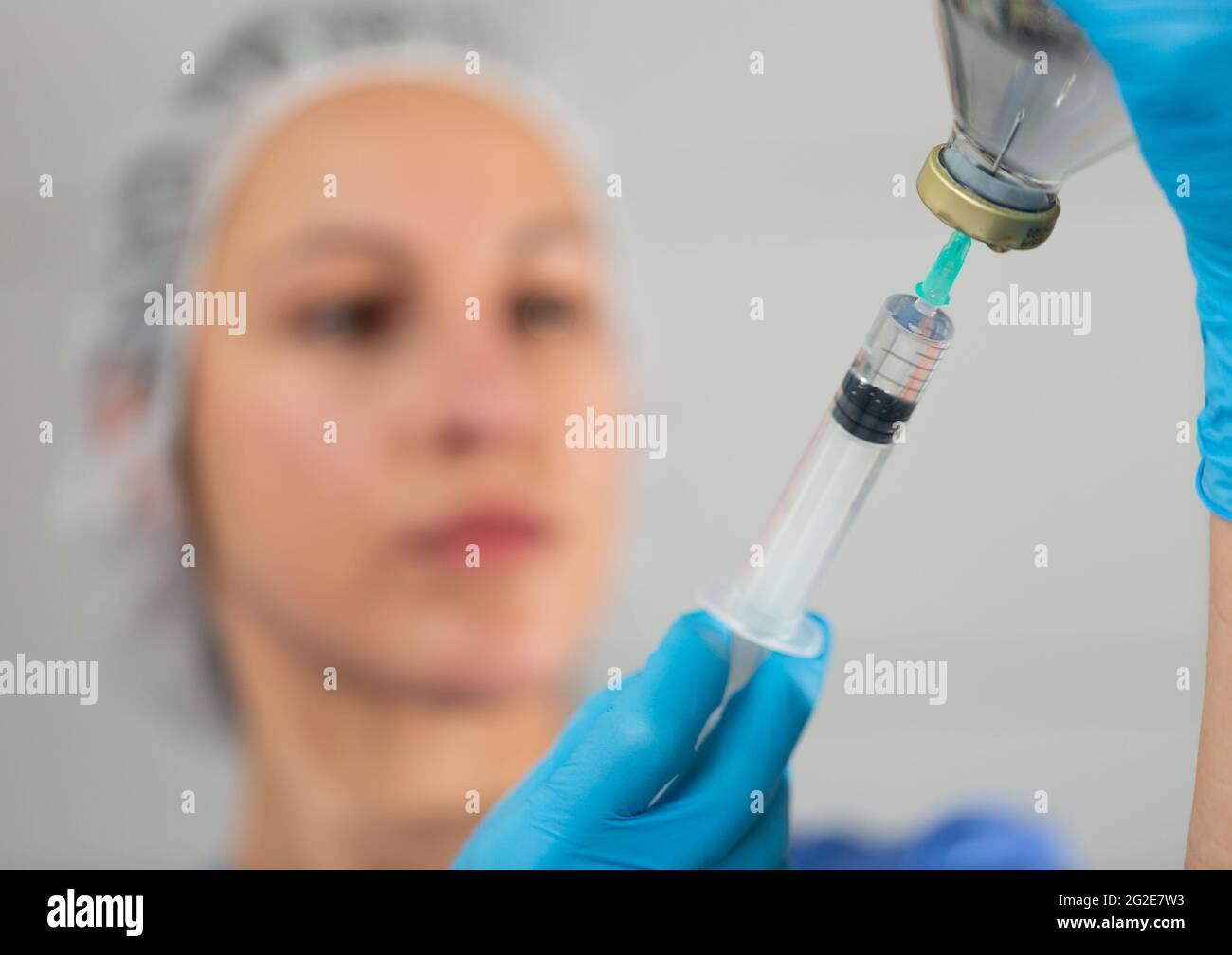 Young female health worker fills a syringe with saline for injection in ...