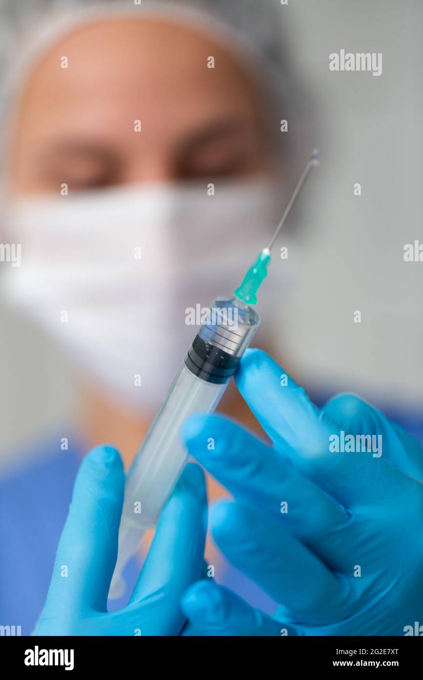 Masked female healthworker prepared a syringe for injection, filling it ...