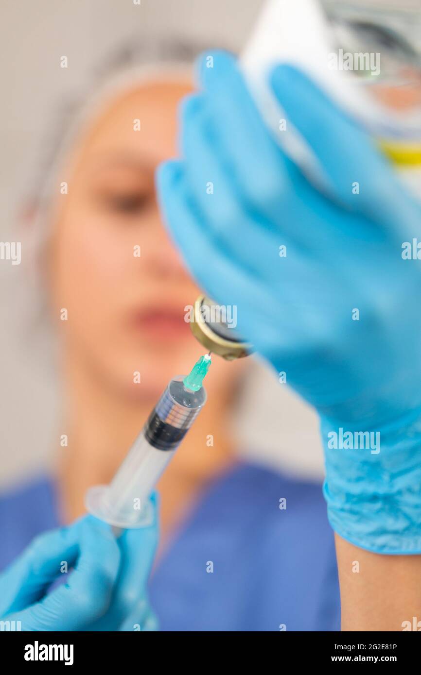 Young female health worker fills a syringe with saline for injection in ...