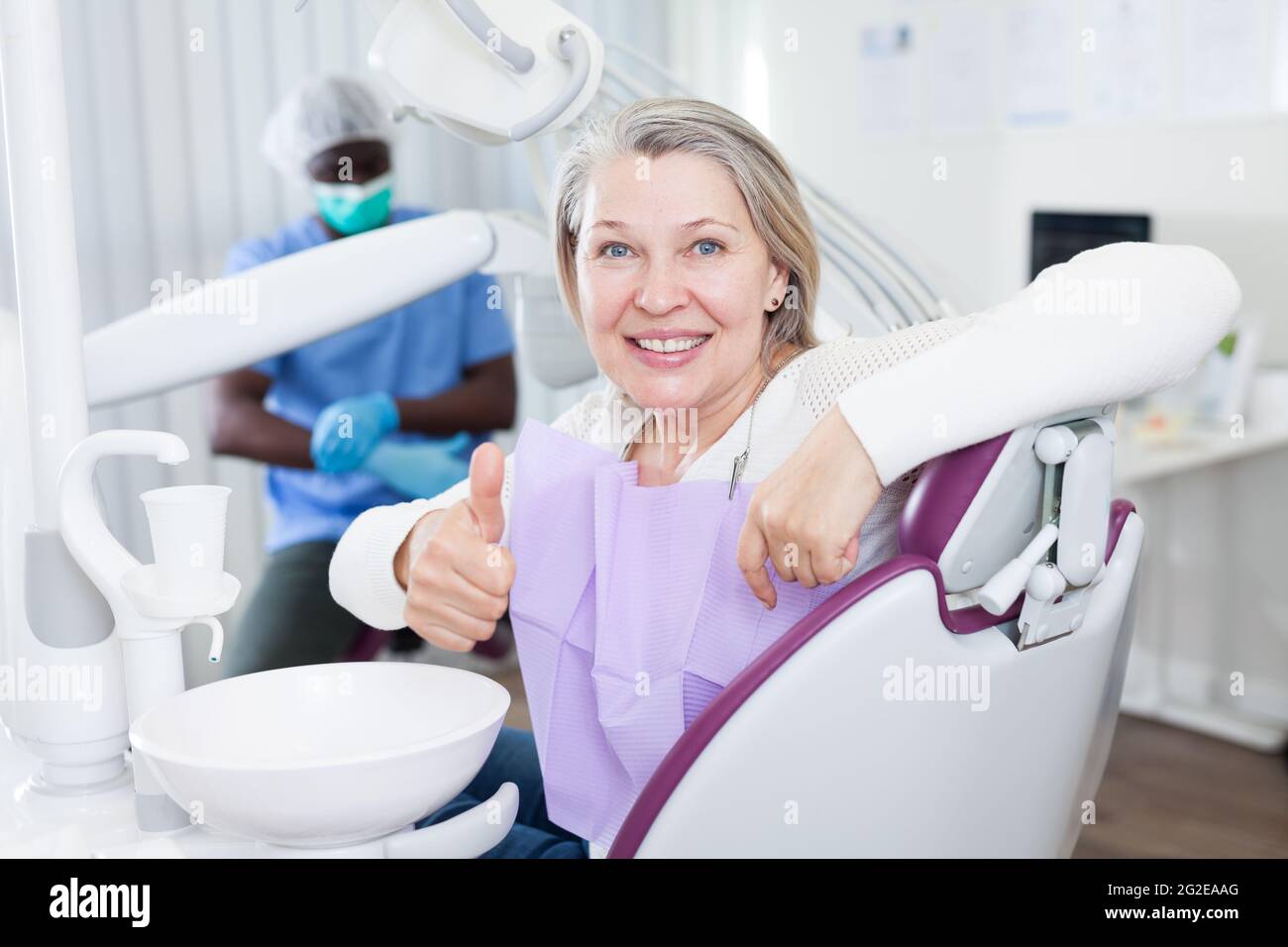 Happy cute mature woman sitting in dental chair after teeth cure giving ...