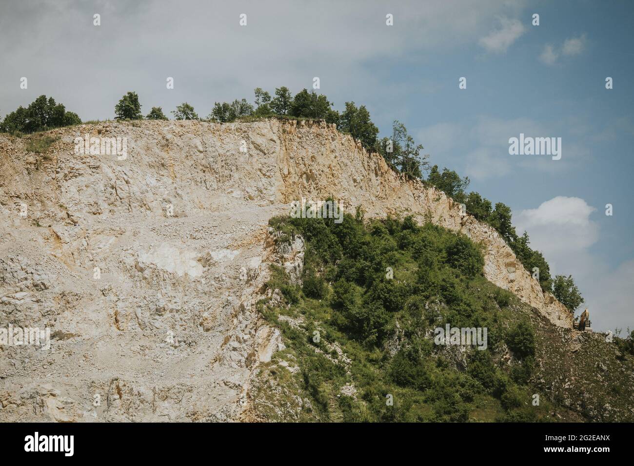 Low angle shot of a cliff with trees on it under a sunny sky filled ...