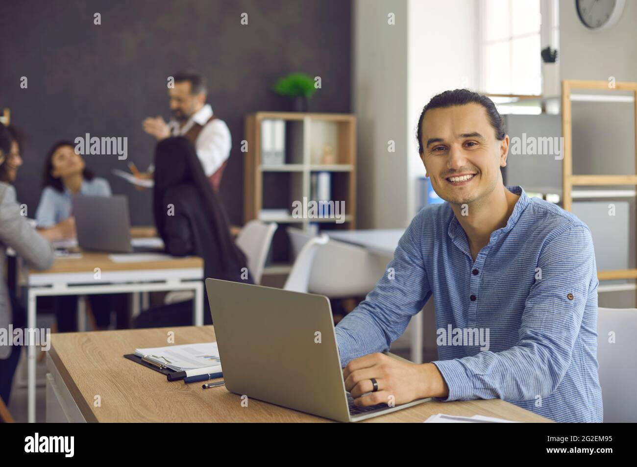 Portrait of happy young business man sitting at office desk with laptop ...