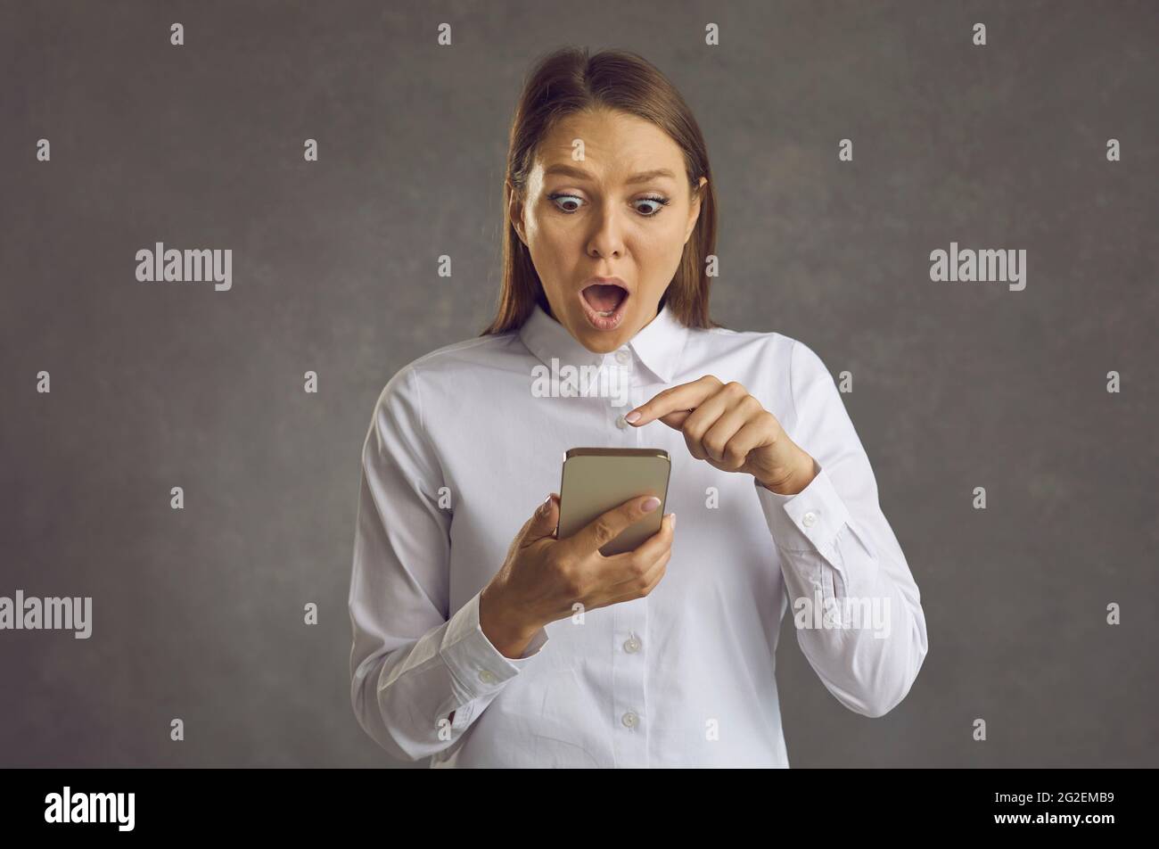 Young woman looking at the screen of her smartphone with a shocked face ...
