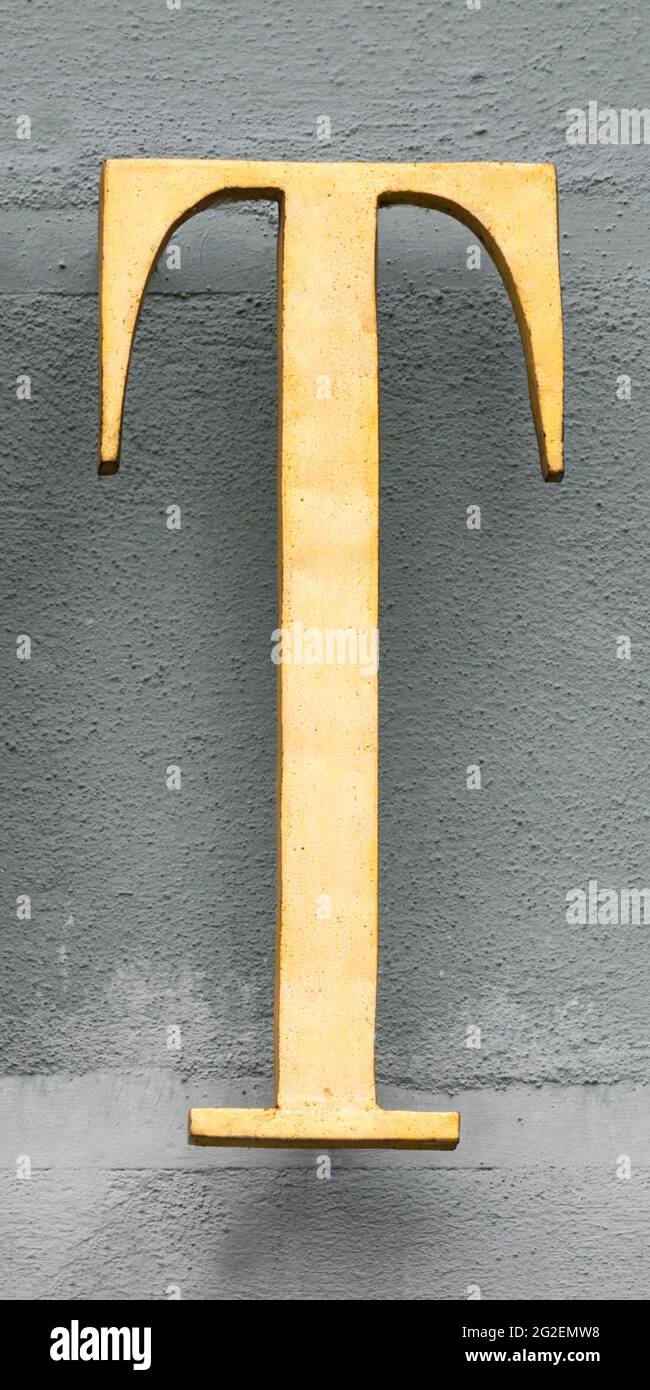 Golden letter T floating in front of grey house wall Stock Photo - Alamy
