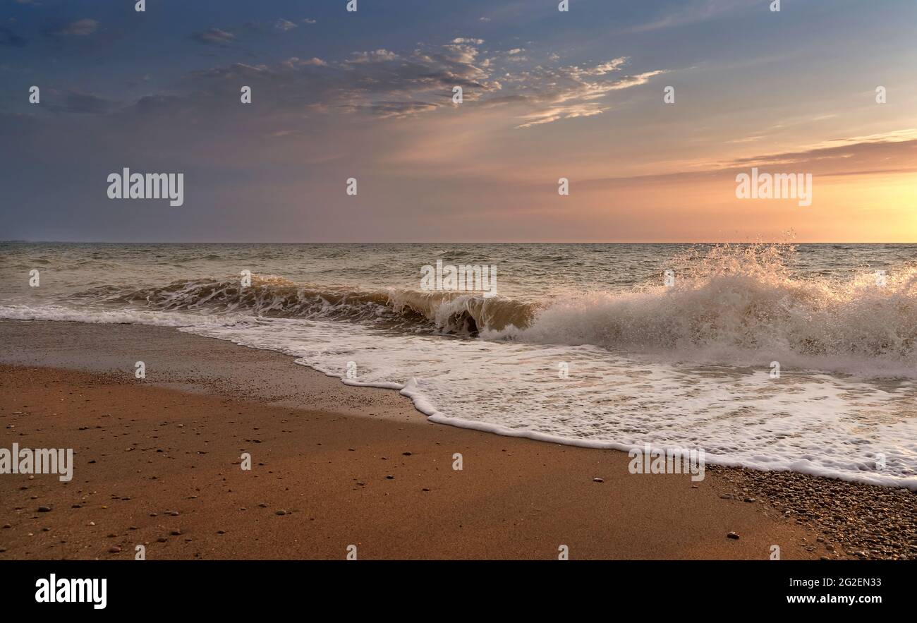 Green blue sea splashing waves backlit by setting sun in front of ...