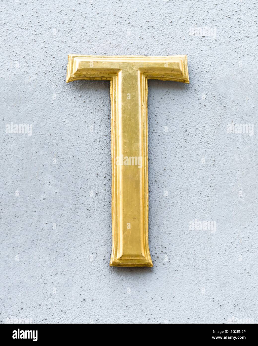 Golden letter T on a light grey wall Stock Photo - Alamy