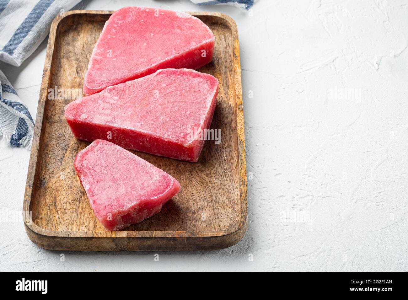 Frozen tuna fish steaks set, on wooden tray, on white stone background ...
