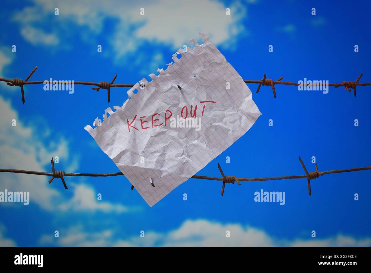 piece of paper with keep out text on barbed wire on blue sky background ...