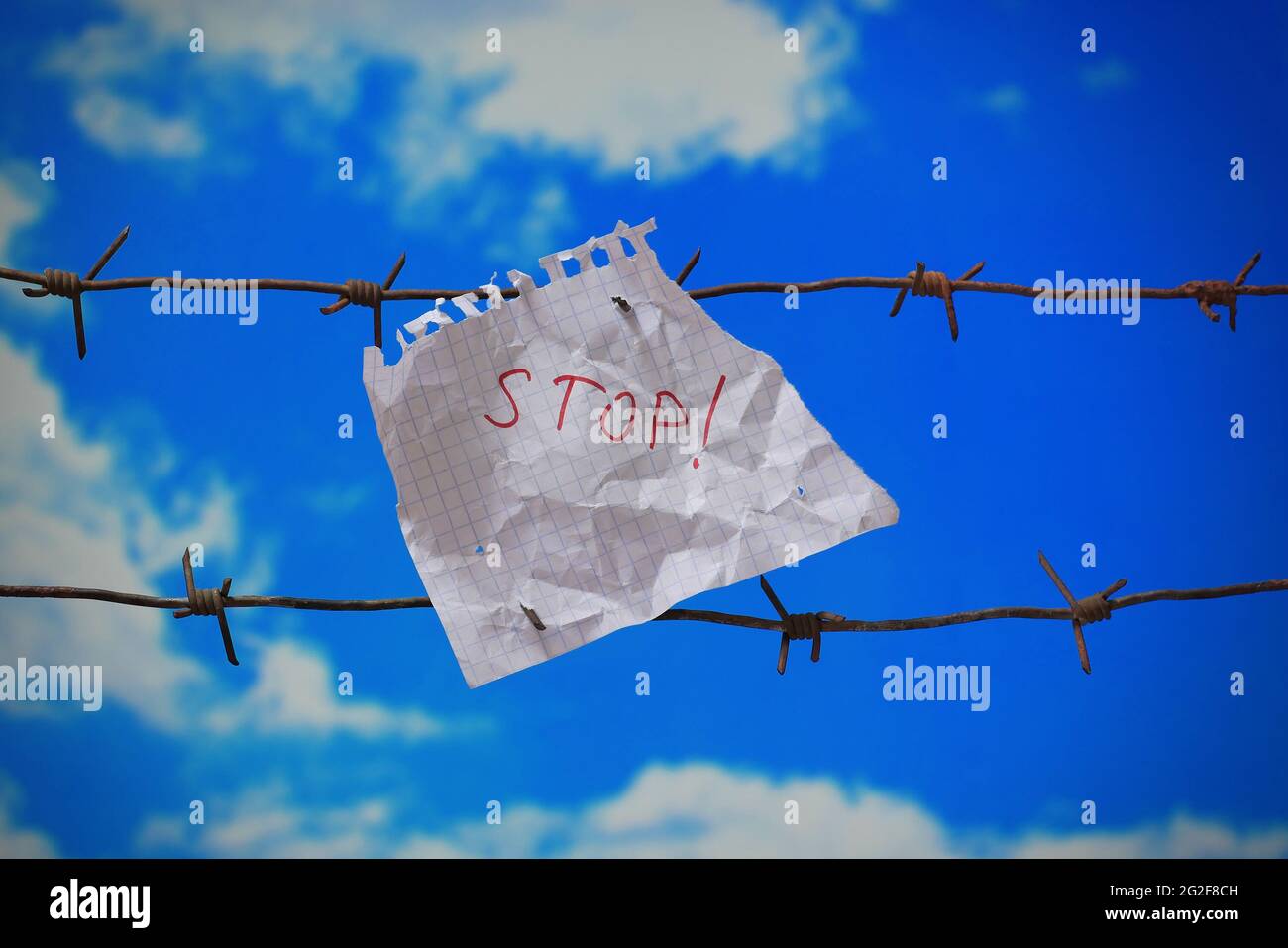 piece of paper with stop text on barbed wire on blue sky background ...